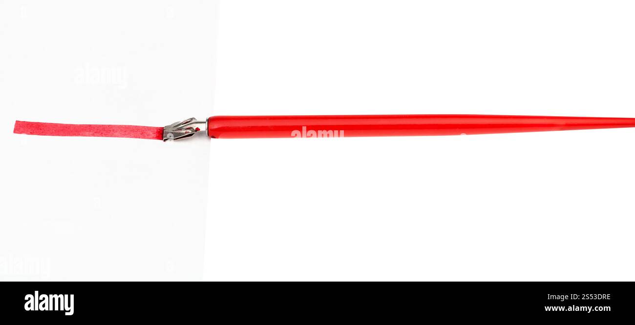 side view of red dip pen drawing a red line on sheet of paper by wide ...