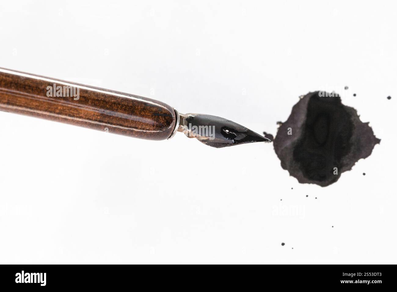 top view of black painted nib of brown penholder over ink blot on white ...