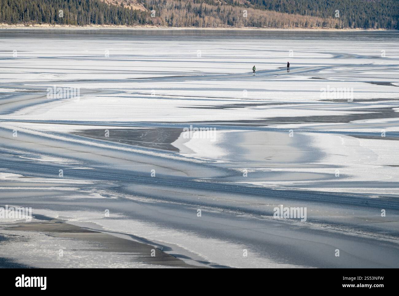 Snow patterns and two ice skaters on frozen Lake Minnewanka in Banff ...