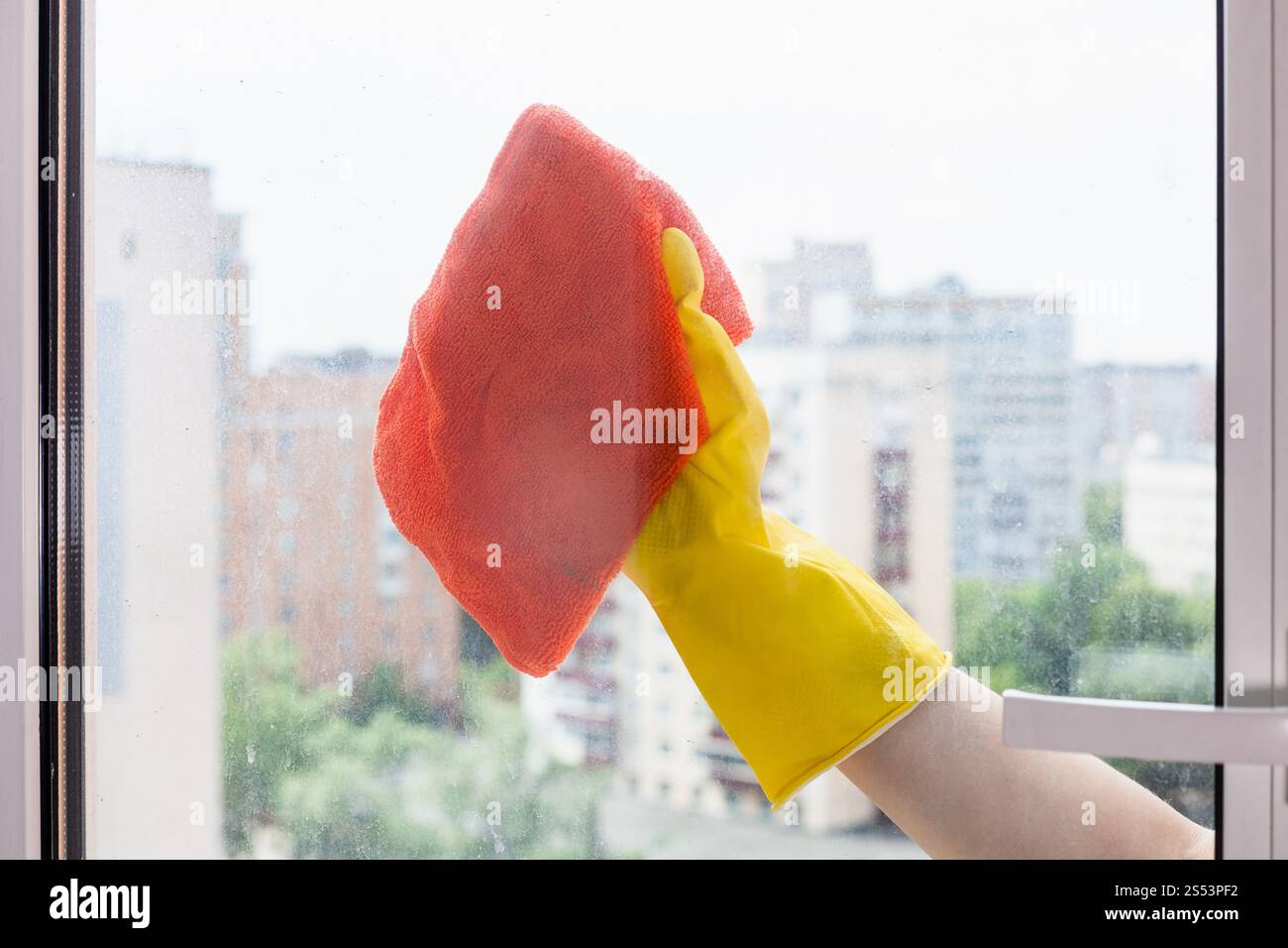cleaning glass of home window in urban apartment house by orange rag ...