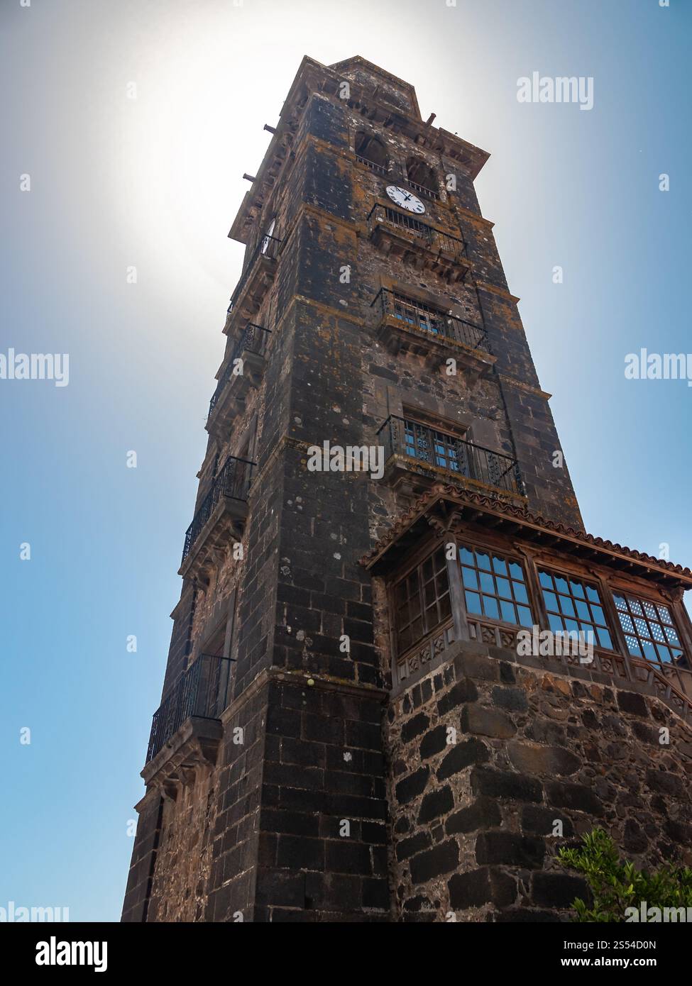 Photo of high stone ancient clock tower against bright sun and blue sky ...