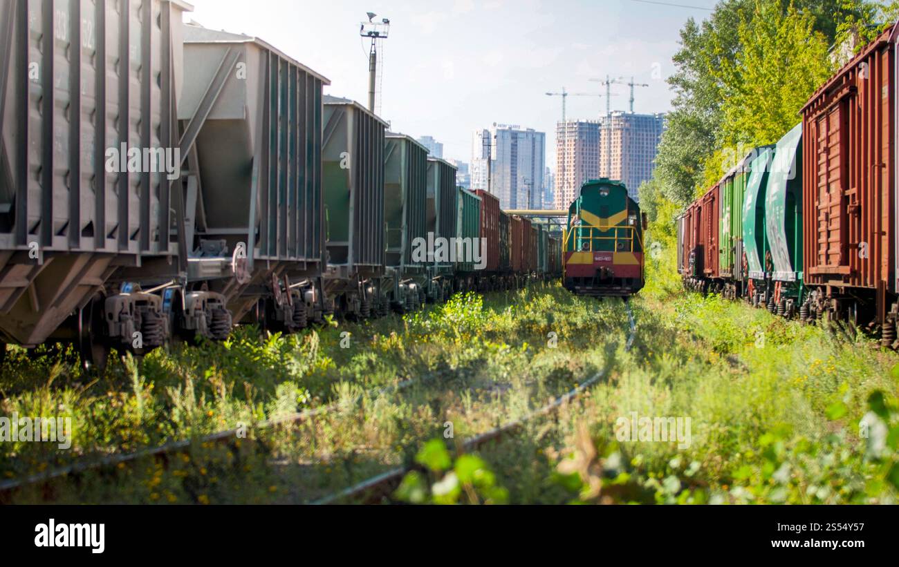 Diesel train riding on railroad between rows of cargo wagons and cars ...