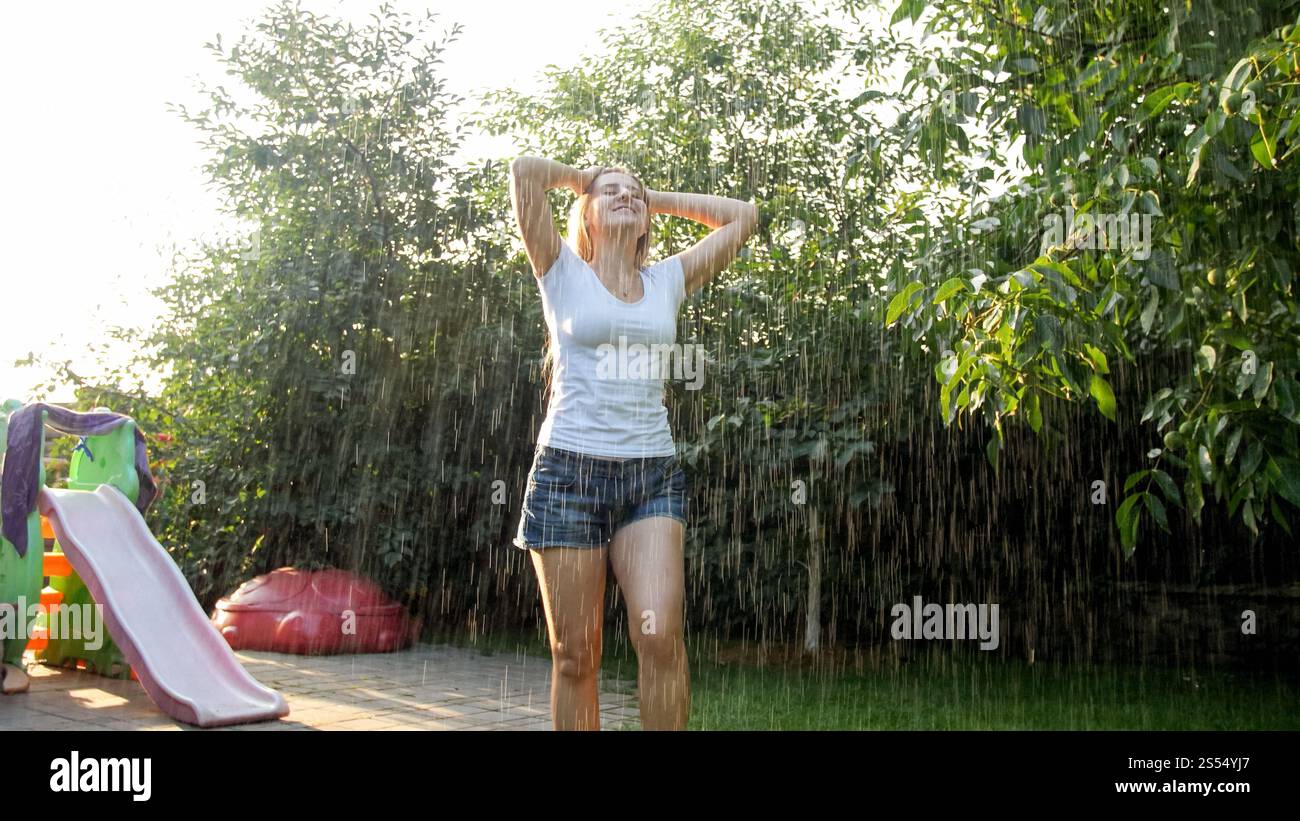 Portrait of laughing young woman with long hair in wet clothes dancing ...