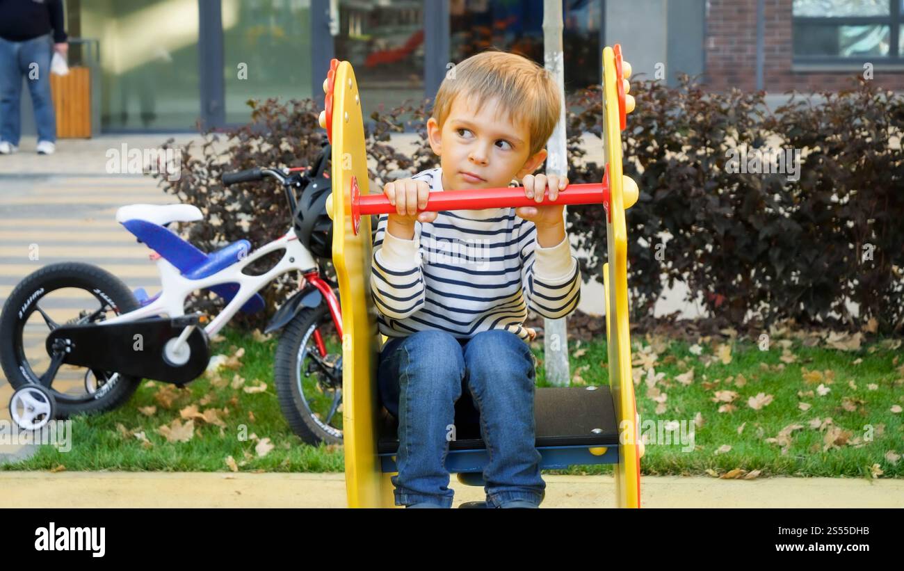 Portrait of thoughtful little boy itting on children playground at park ...