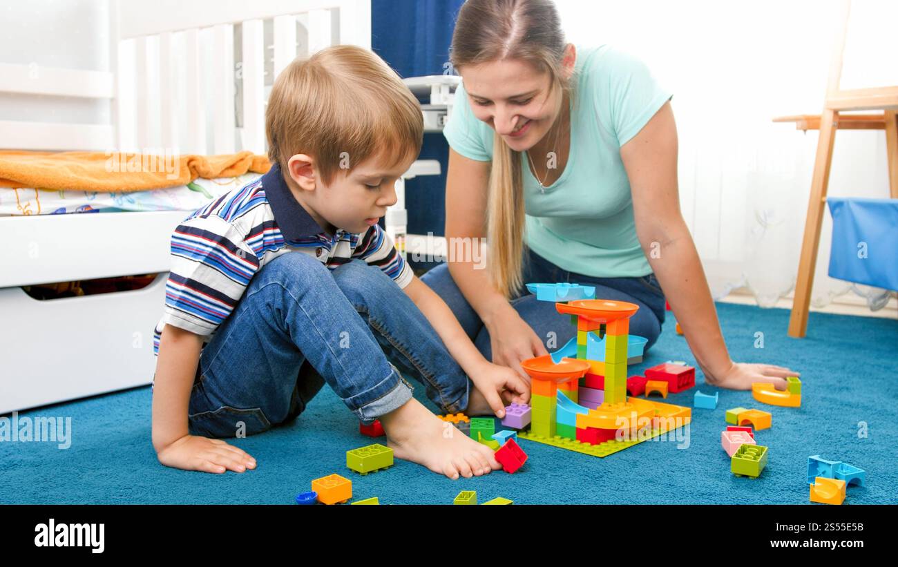 Beautiful young woman helping her toddler son building colorful plastic ...