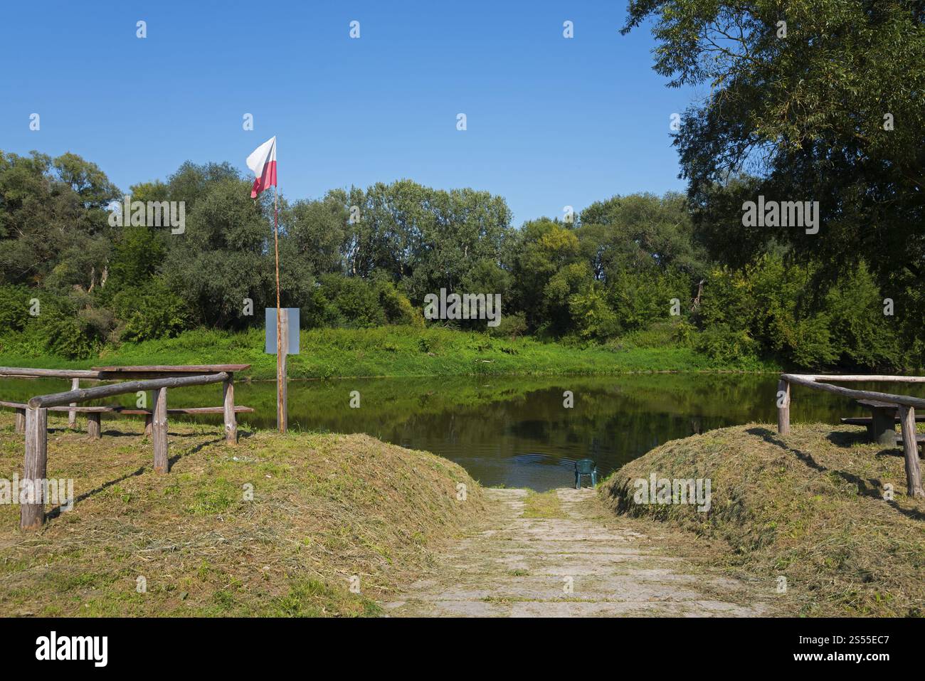 Riverbank with Polish flag and wooden railing, surrounded by green ...