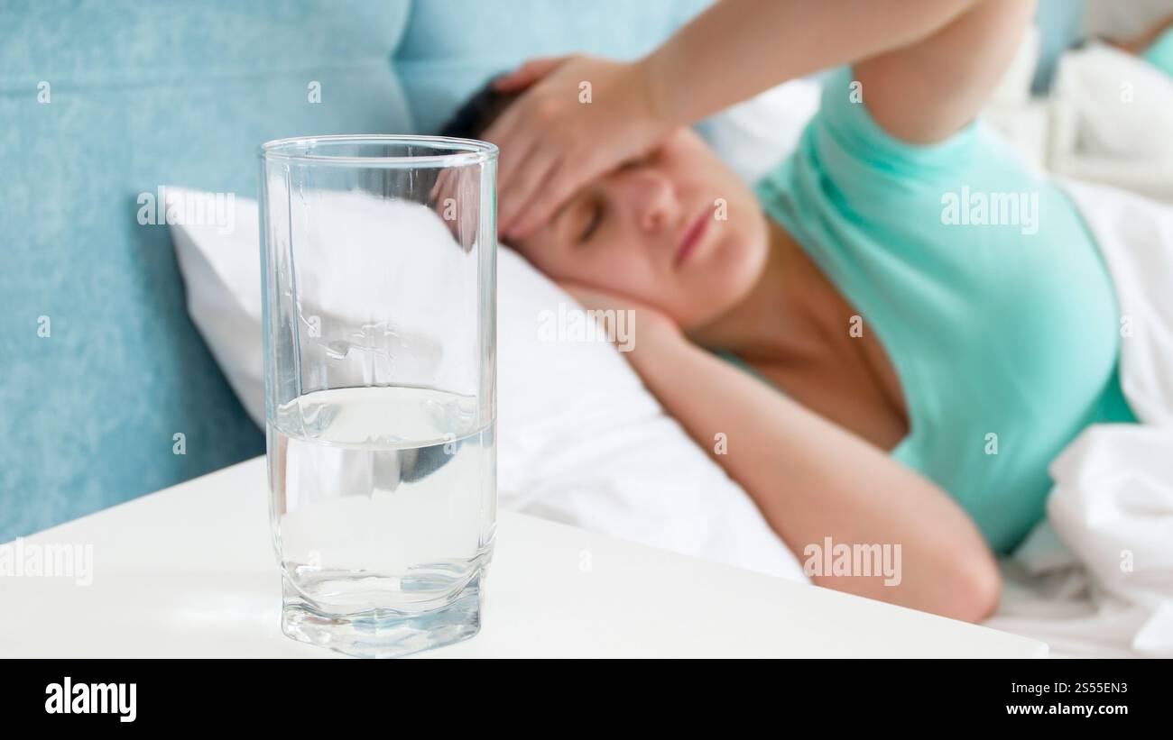 Glass of water on the bedside table against sick woman with migraine ...
