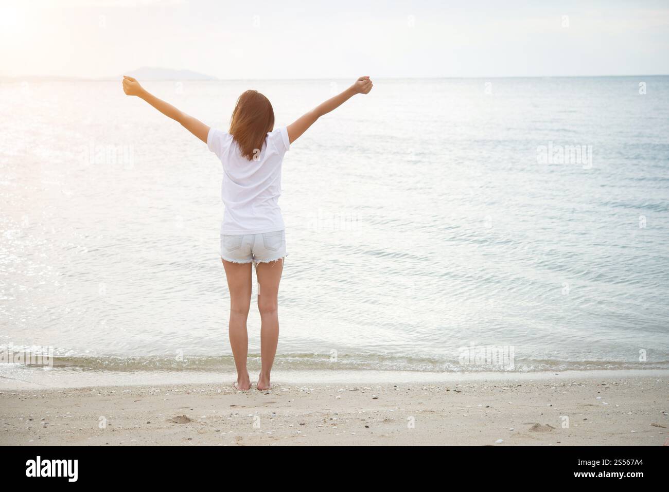 Rear of young woman standing stretch her arms in the air on the beach ...