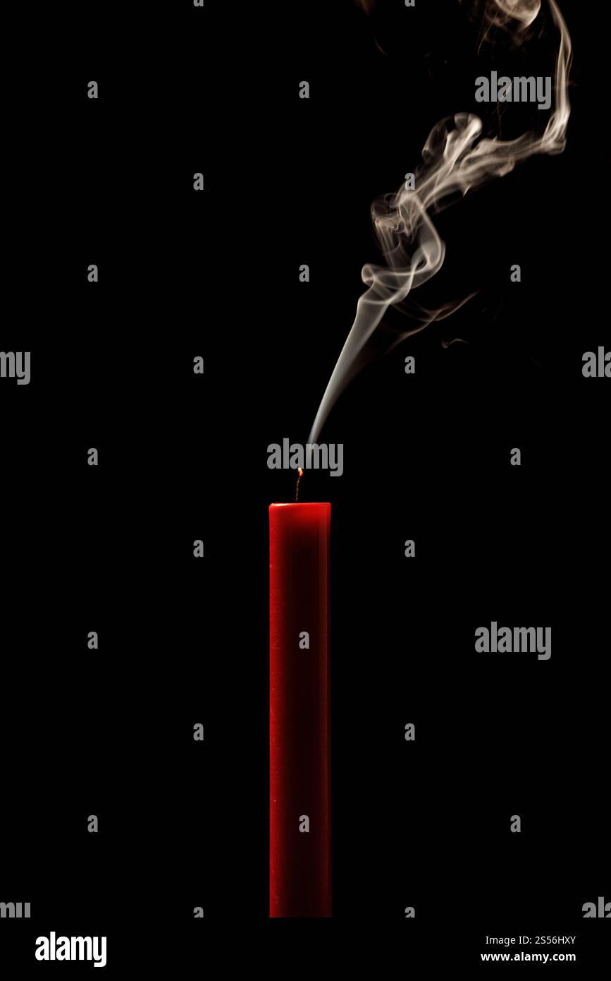 Smoke trail rising from the wick of a red candle. Black background and ...