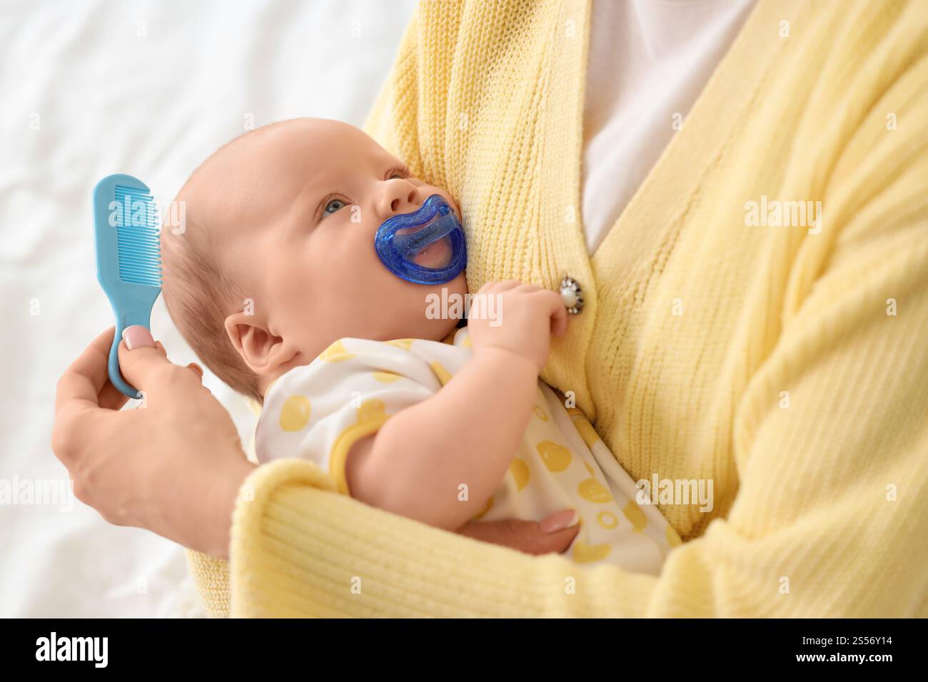 Mother combing her little baby's hair with cradle cap on bed, closeup ...
