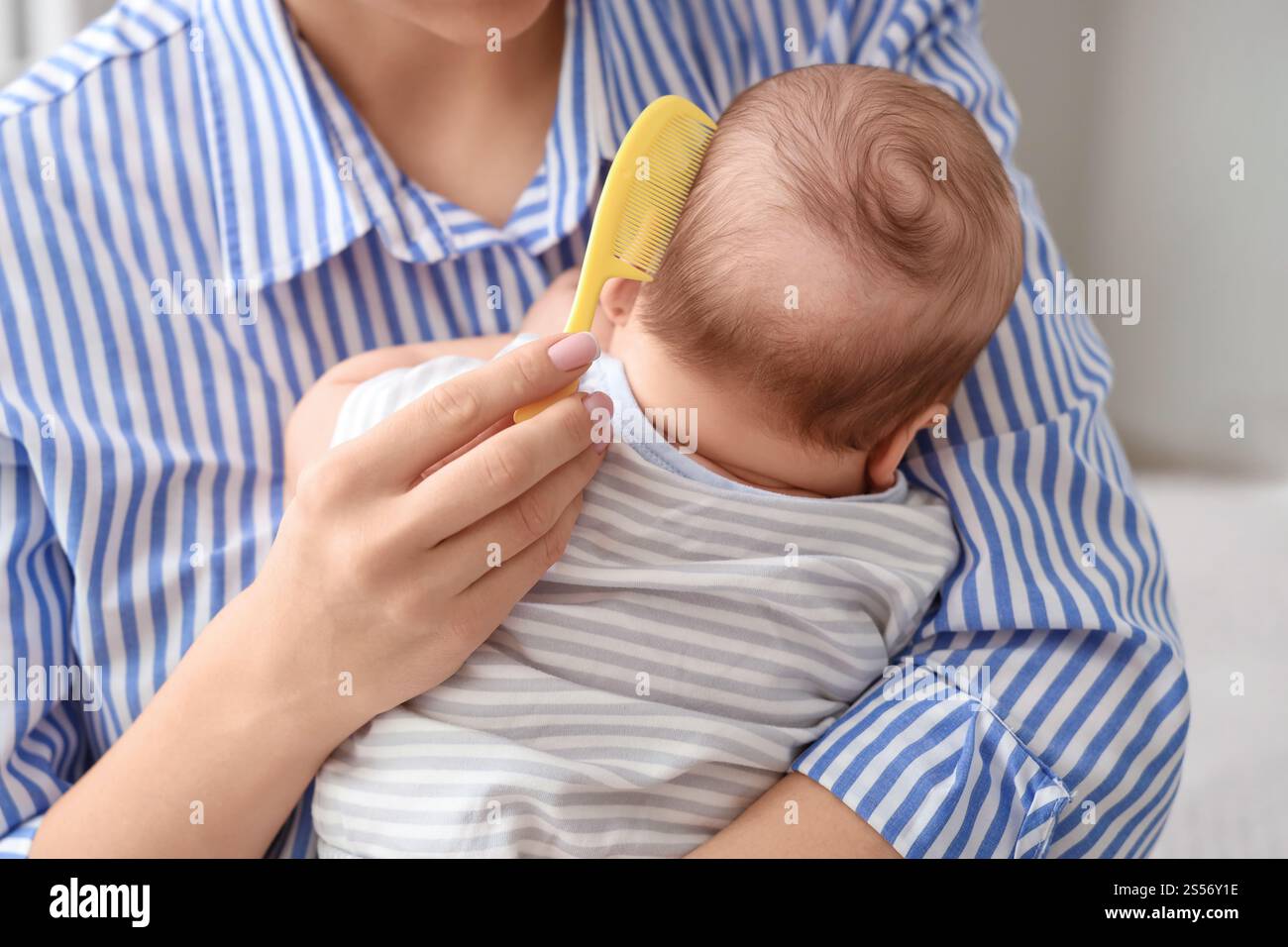 Mother combing her little baby's hair with cradle cap in bedroom ...