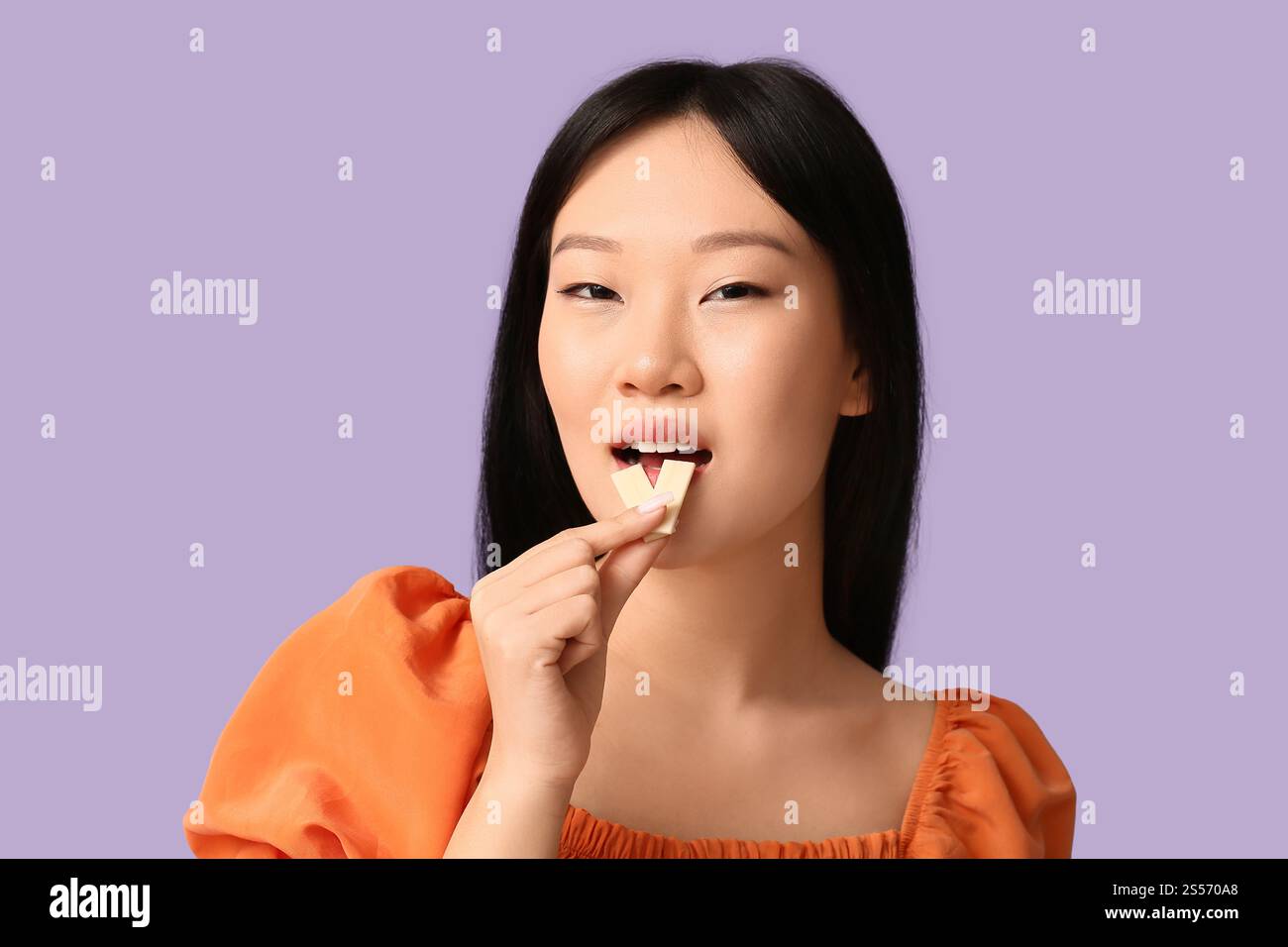 Pretty young Asian woman with open mouth holding chewing gums on lilac ...