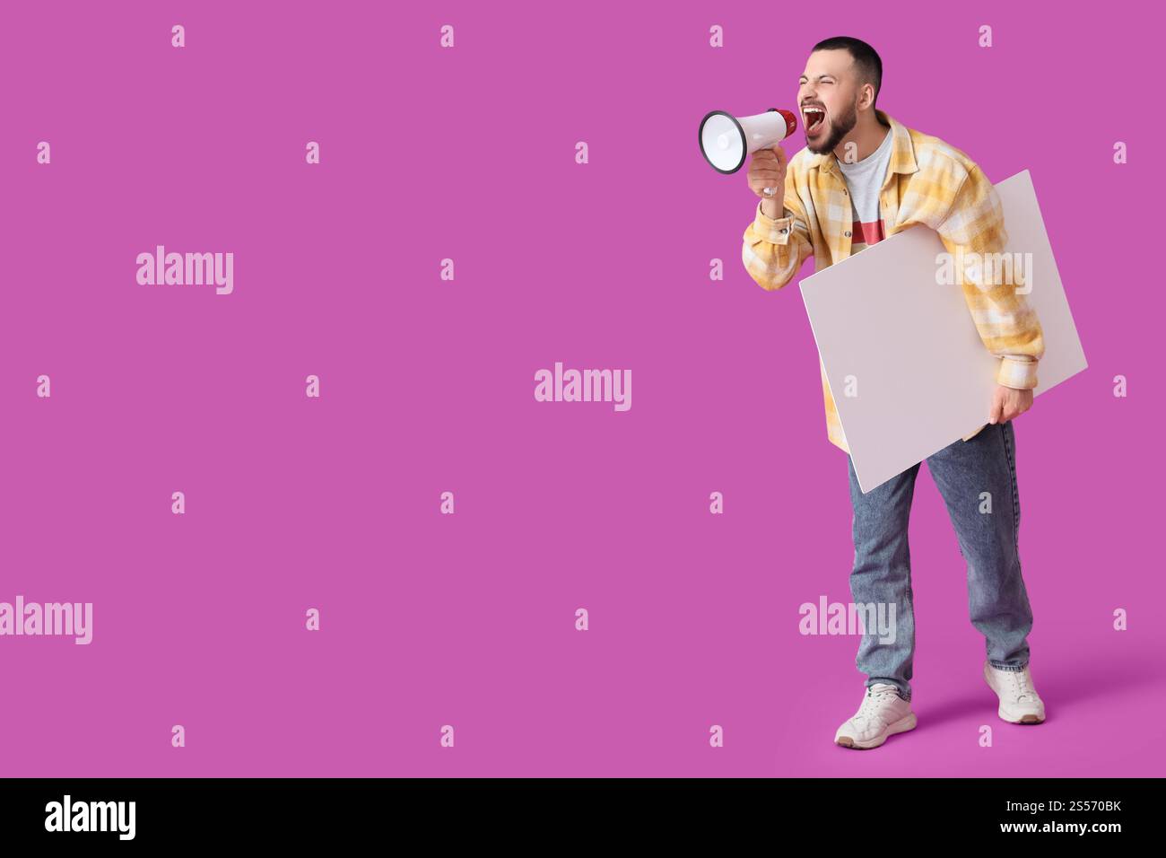 Young man with blank poster shouting into megaphone on violet ...