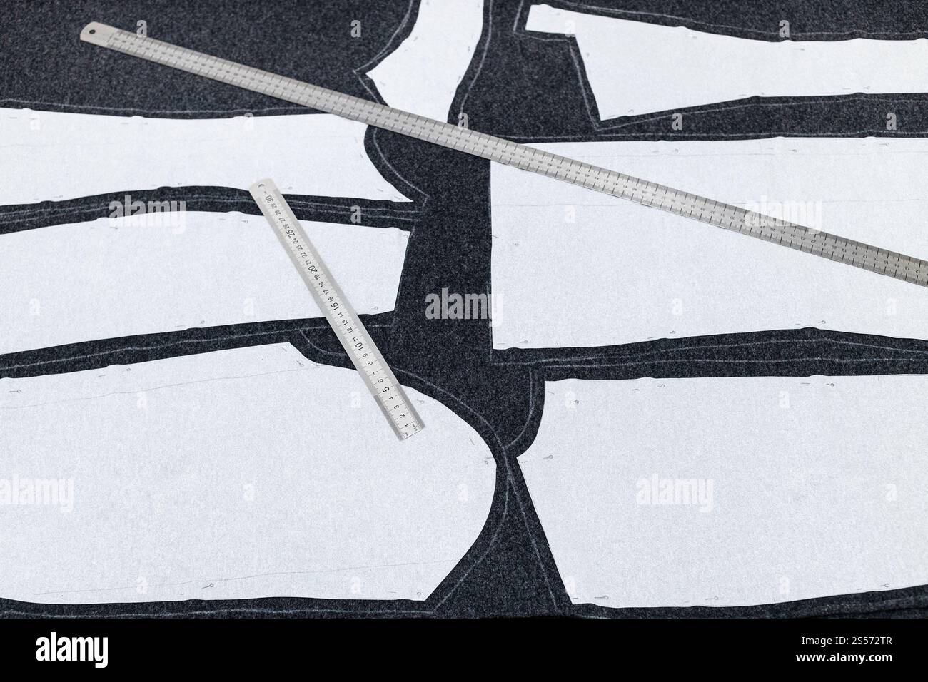 layout of sewing patterns of dress and steel rulers on dark fabric ...