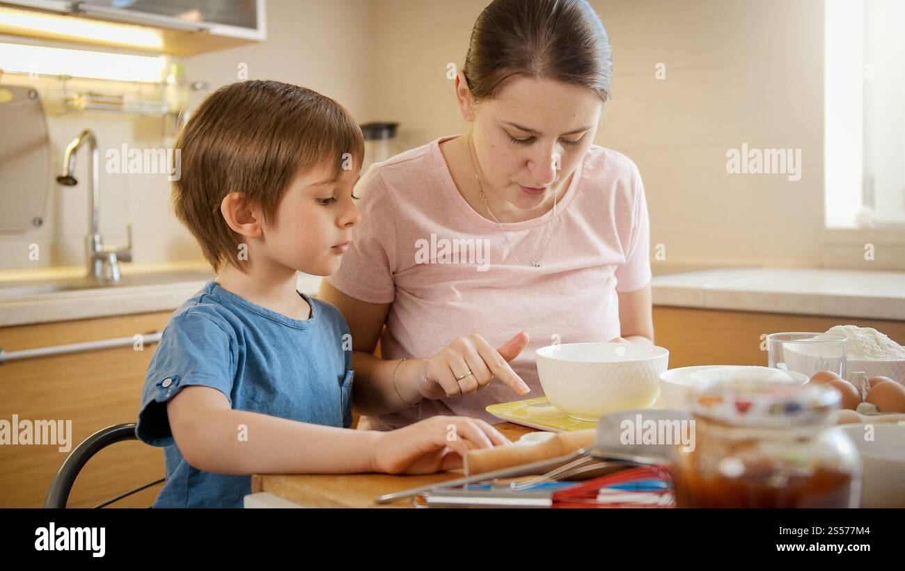 Young mother checking recipe on smartphone while baking pie or cake ...