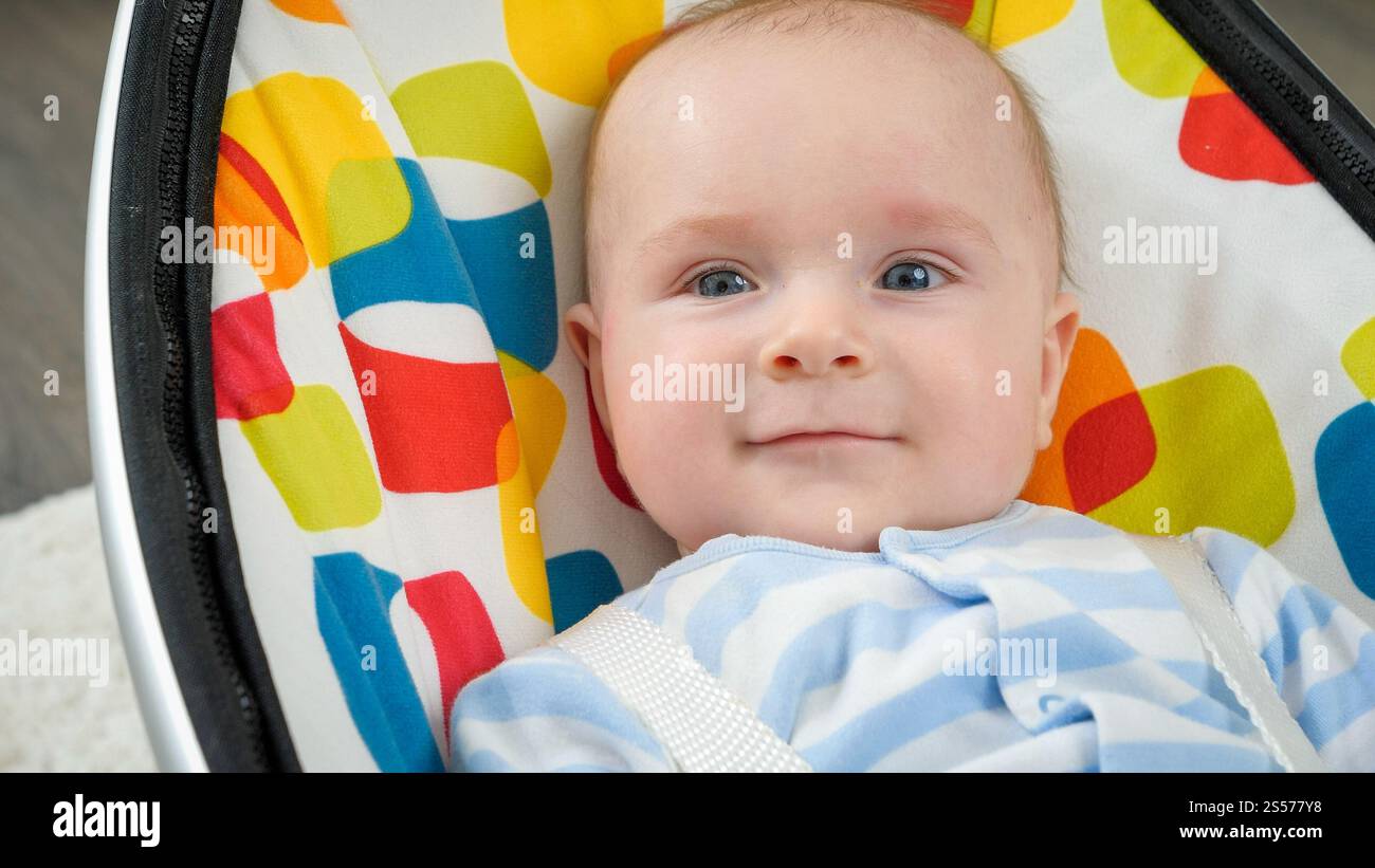 Smiling baby boy looking in camera while rocking in colorful chair ...