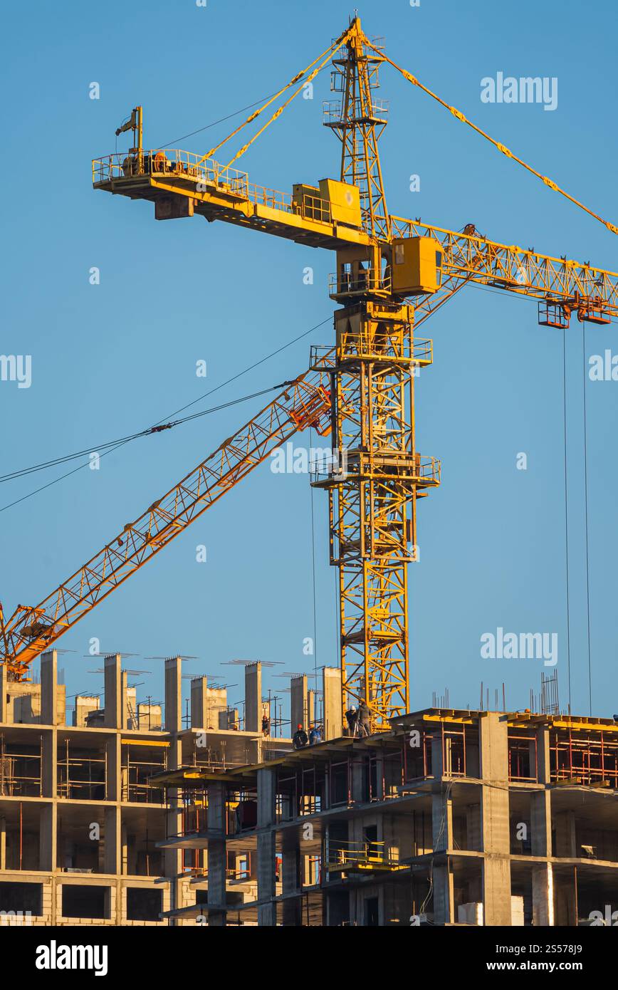 Yellow tower crane working on building construction site, lifting heavy ...
