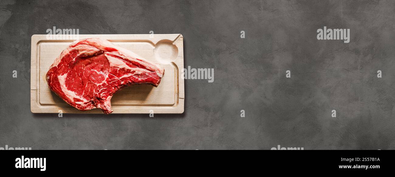 Raw beef prime rib and wooden cutting board isolated on dark concrete ...
