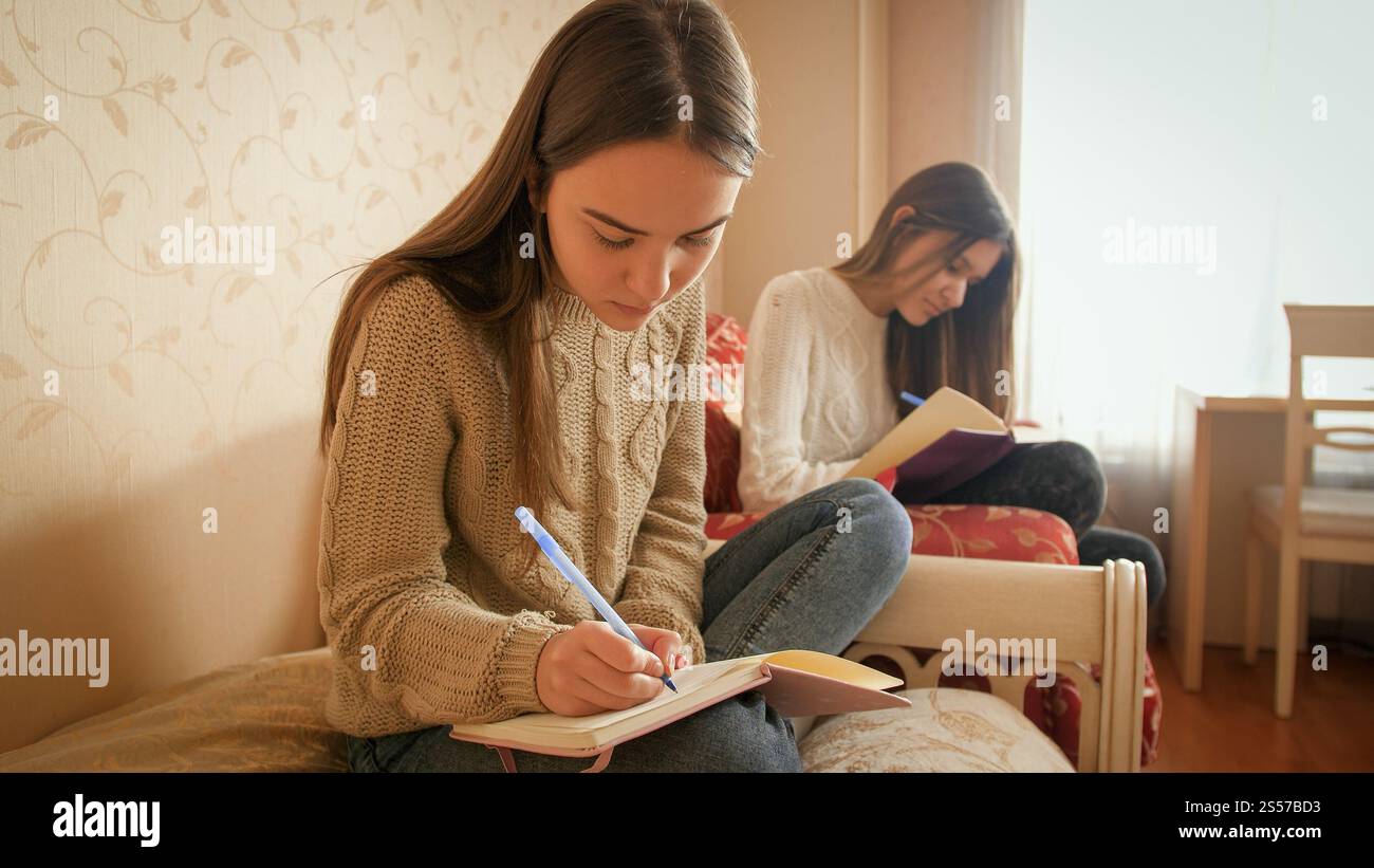 Two teenage sister doing homework and writing in copybooks. Teens ...