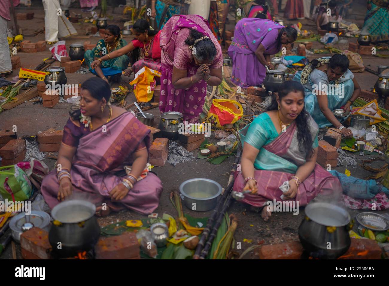 A Tamil woman offers prayers as other cook special food to celebrate ...