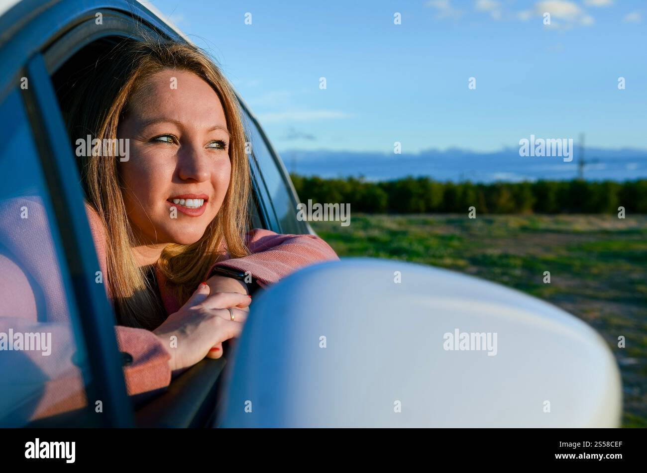 Businesswoman smiles while enjoying road trip, leaning out car window ...