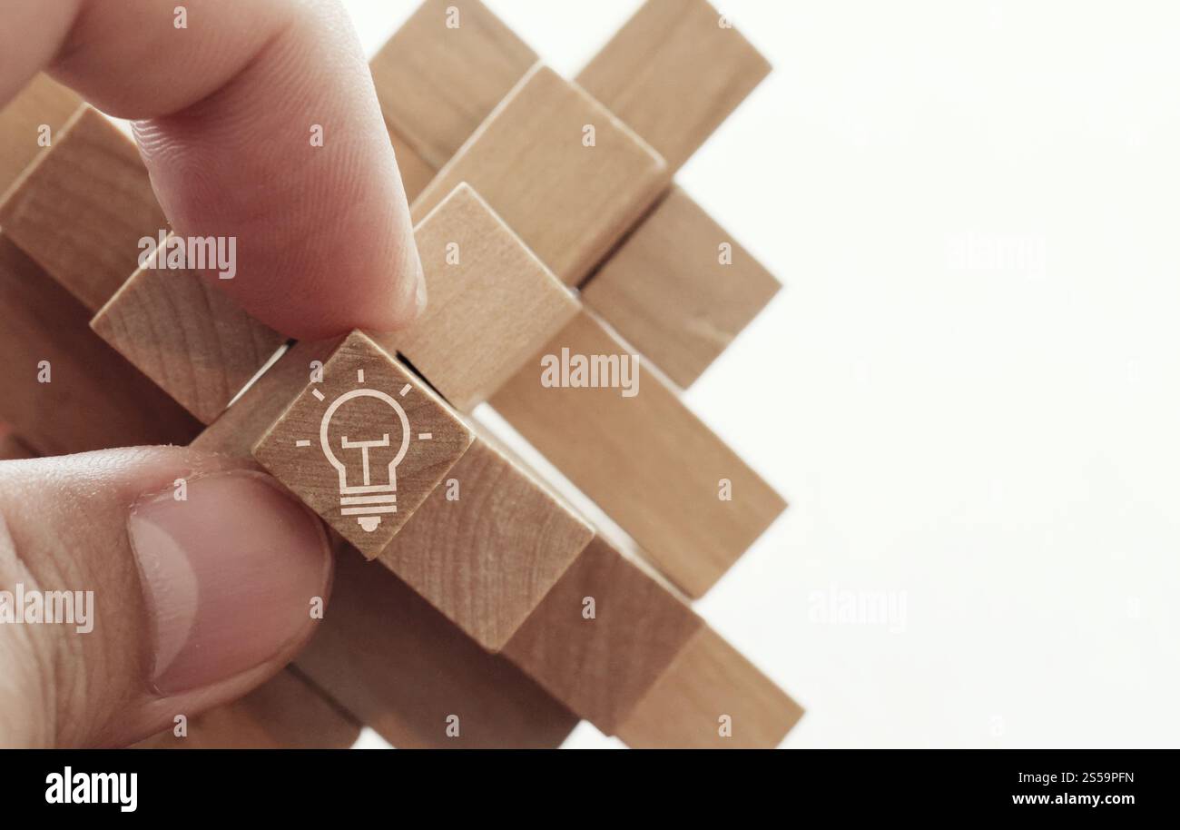 close up of hand showing illuminated light bulb icon on a wooden block puzzle as innovation ...