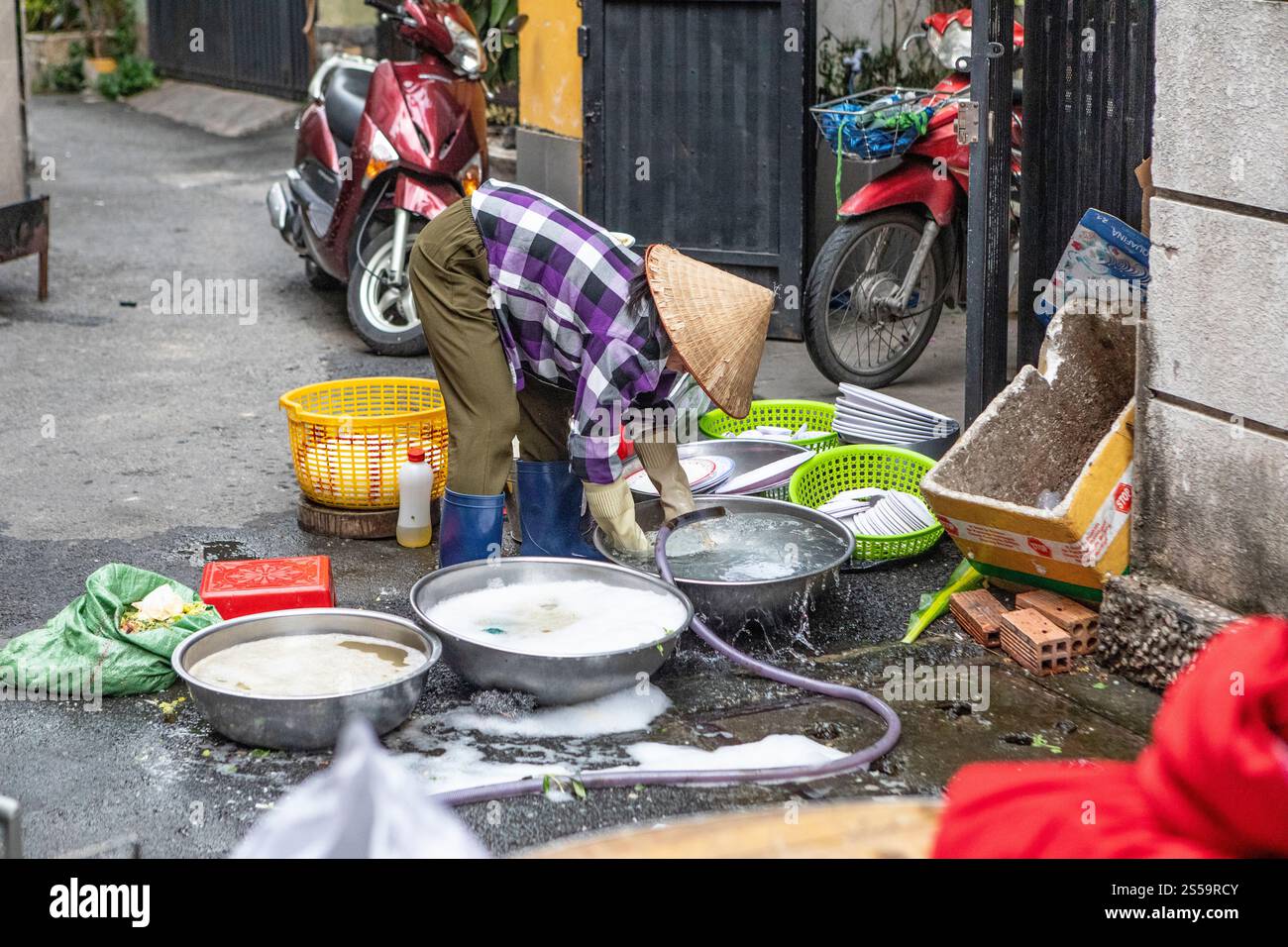 A Vietnamese lady in a traditional Non La conical hat washing plates in ...