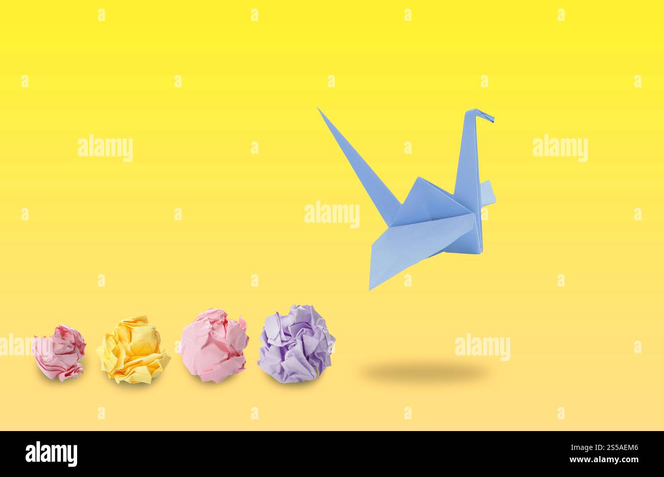 Blue origami crane and crumpled paper balls on yellow gradient ...