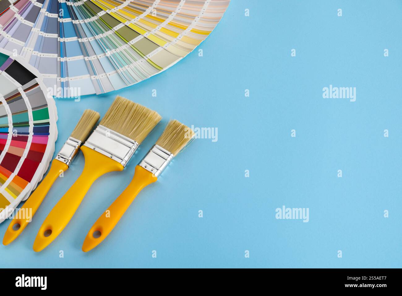 Color selection charts and paint brushes on light blue table, space for ...