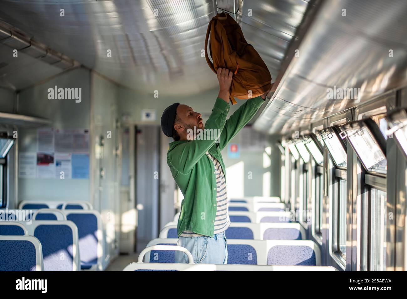 Man tourist lifts backpack onto overhead luggage rack in train. Solo ...