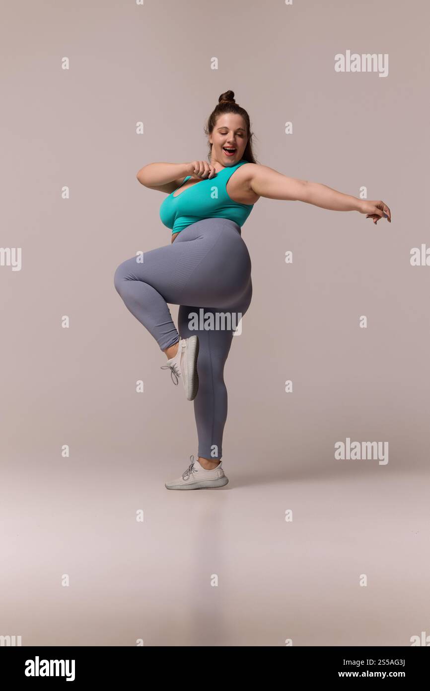 Woman in blue top and leggings raising one leg, smiling joyfully while ...