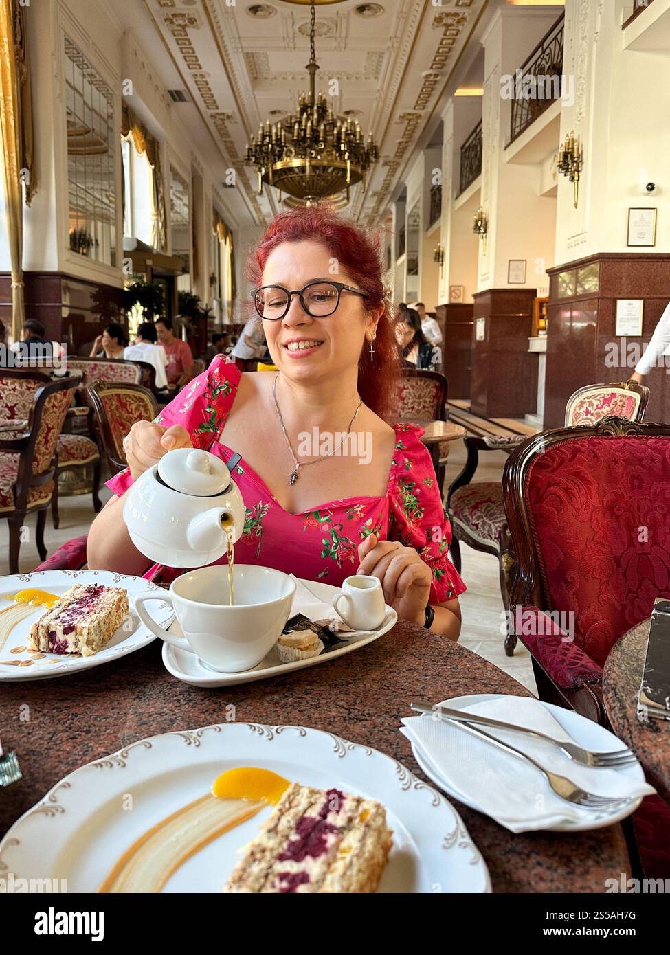 Millennial cheerful woman pouring tea in a luxurious cafe setting with ...
