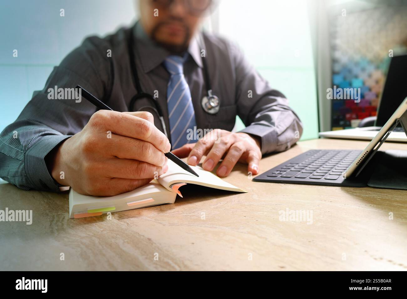 medical doctor writing on notebook and digital tablet docking keyboard ...