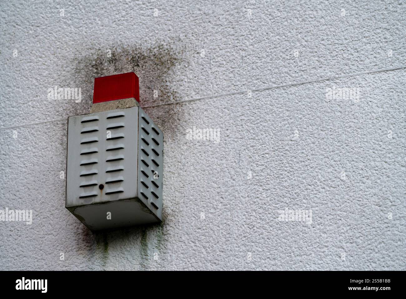A weathered alert system is installed on a textured white wall. It ...