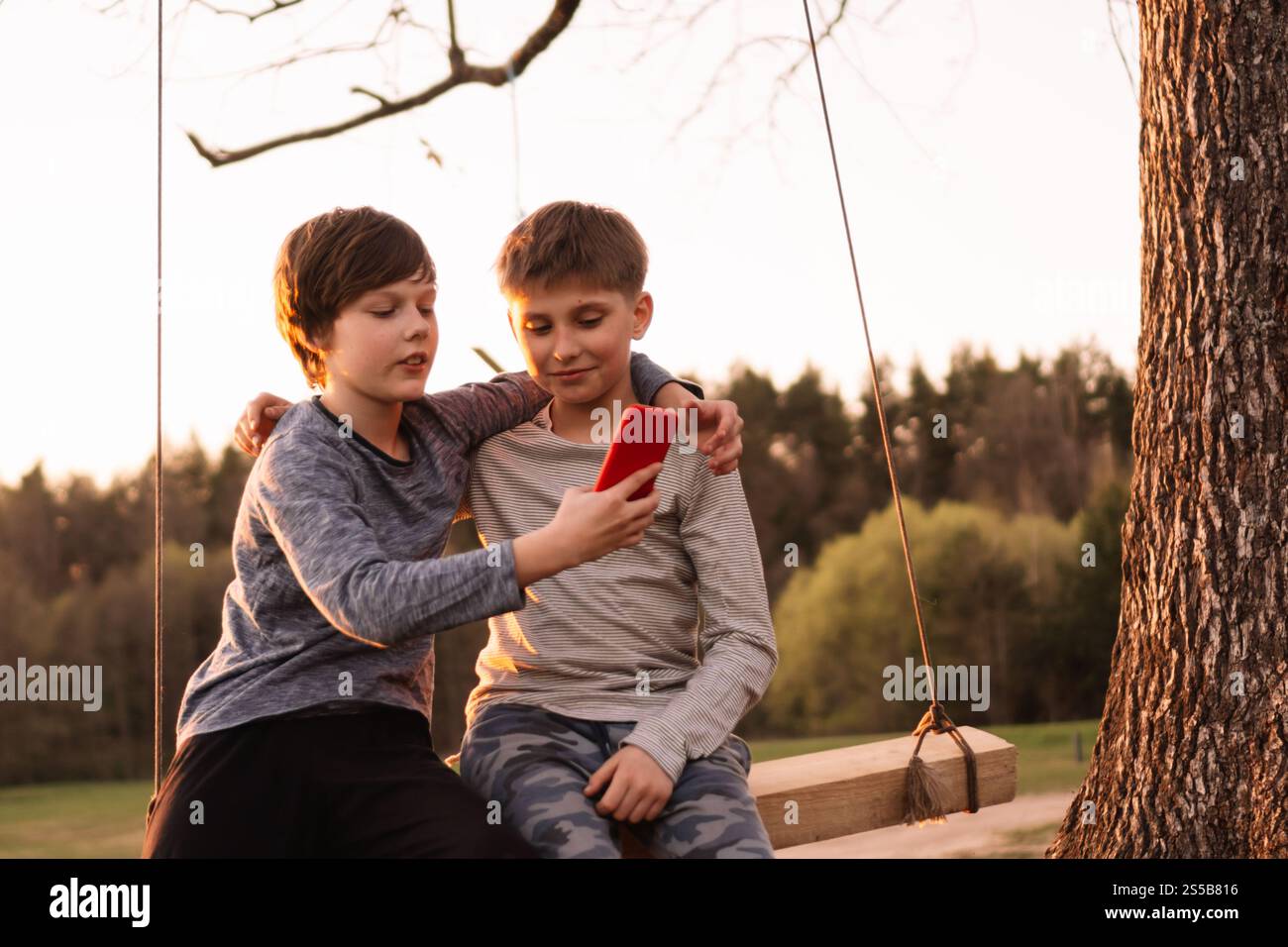 Two teenage friends are sitting on swing in park,hugging and looking at ...