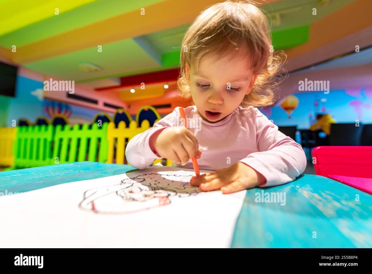 A creative child coloring at a colorful table in a vibrant indoor play ...