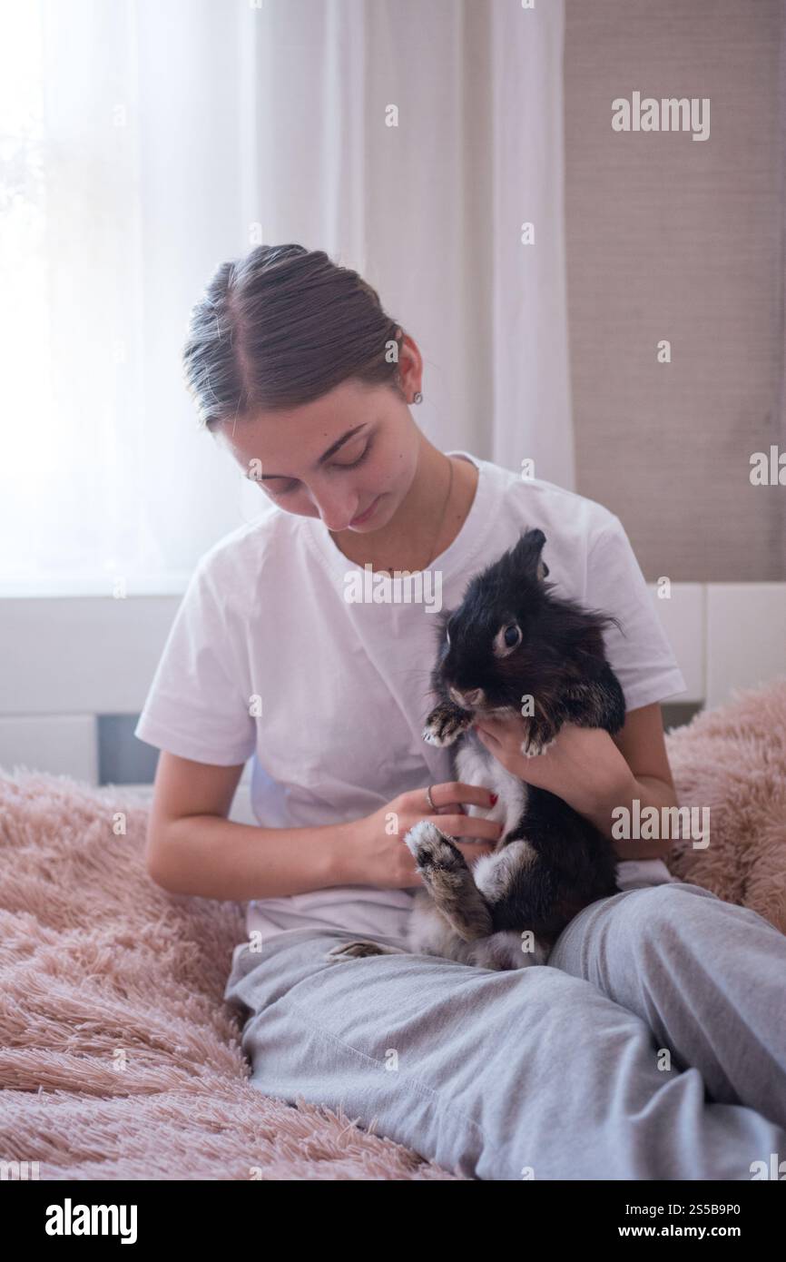 Young woman gently grooming her pet rabbit on a fluffy bed. A moment of ...