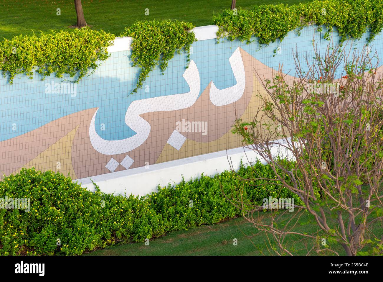 A mural with the Arabic script "Dubai" on a wall surrounded by lush ...