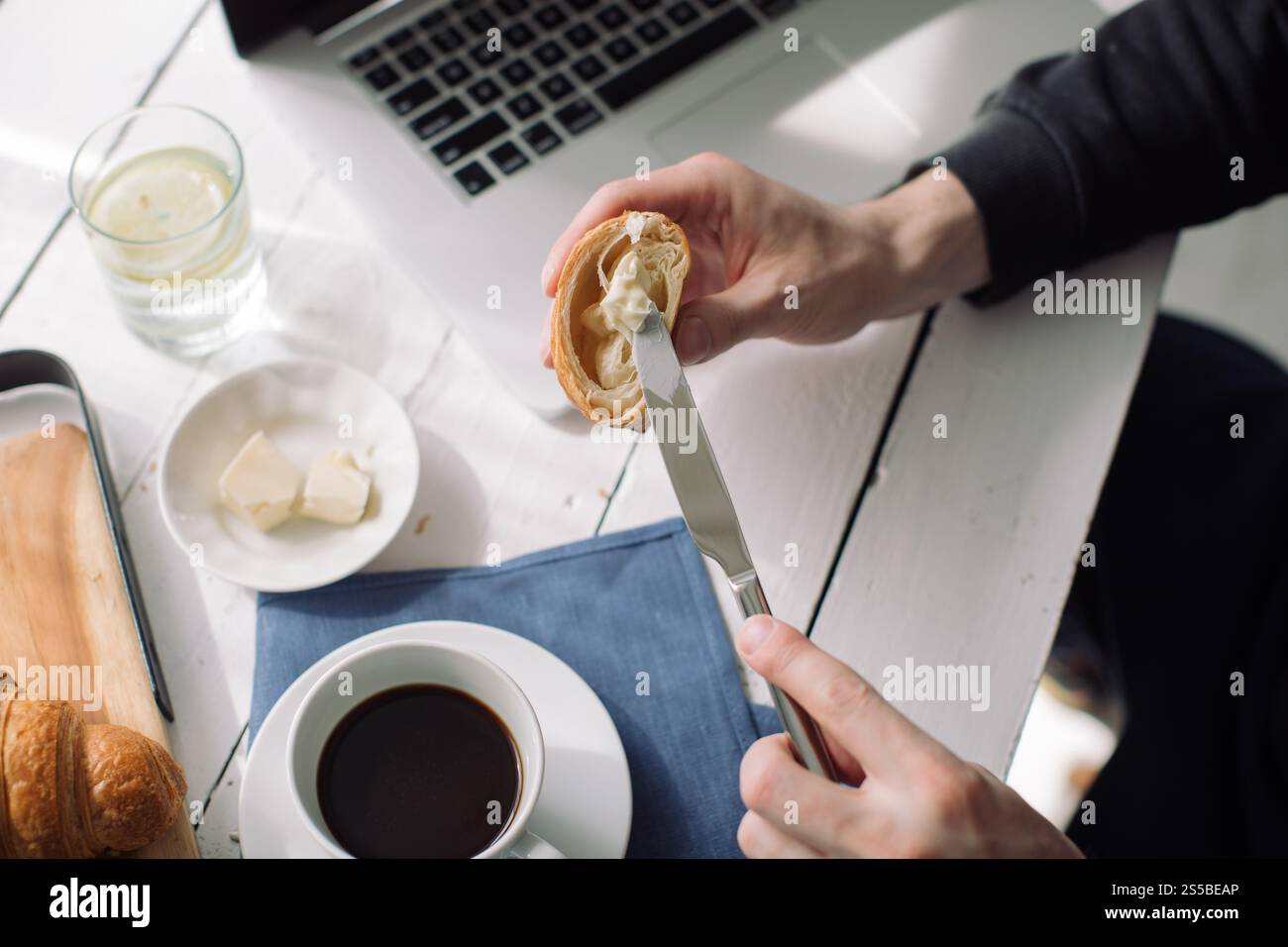 Overhead view of a man buttering a croissant and drinking coffee while ...
