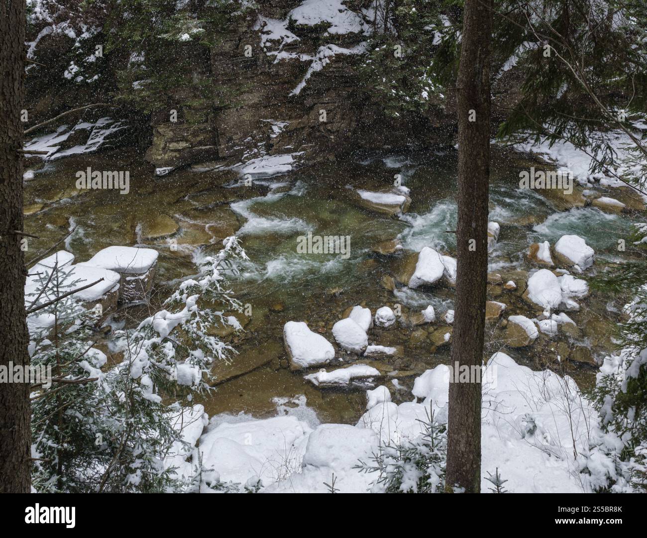 Winter scenery with snowfall and mountain stream running through ...