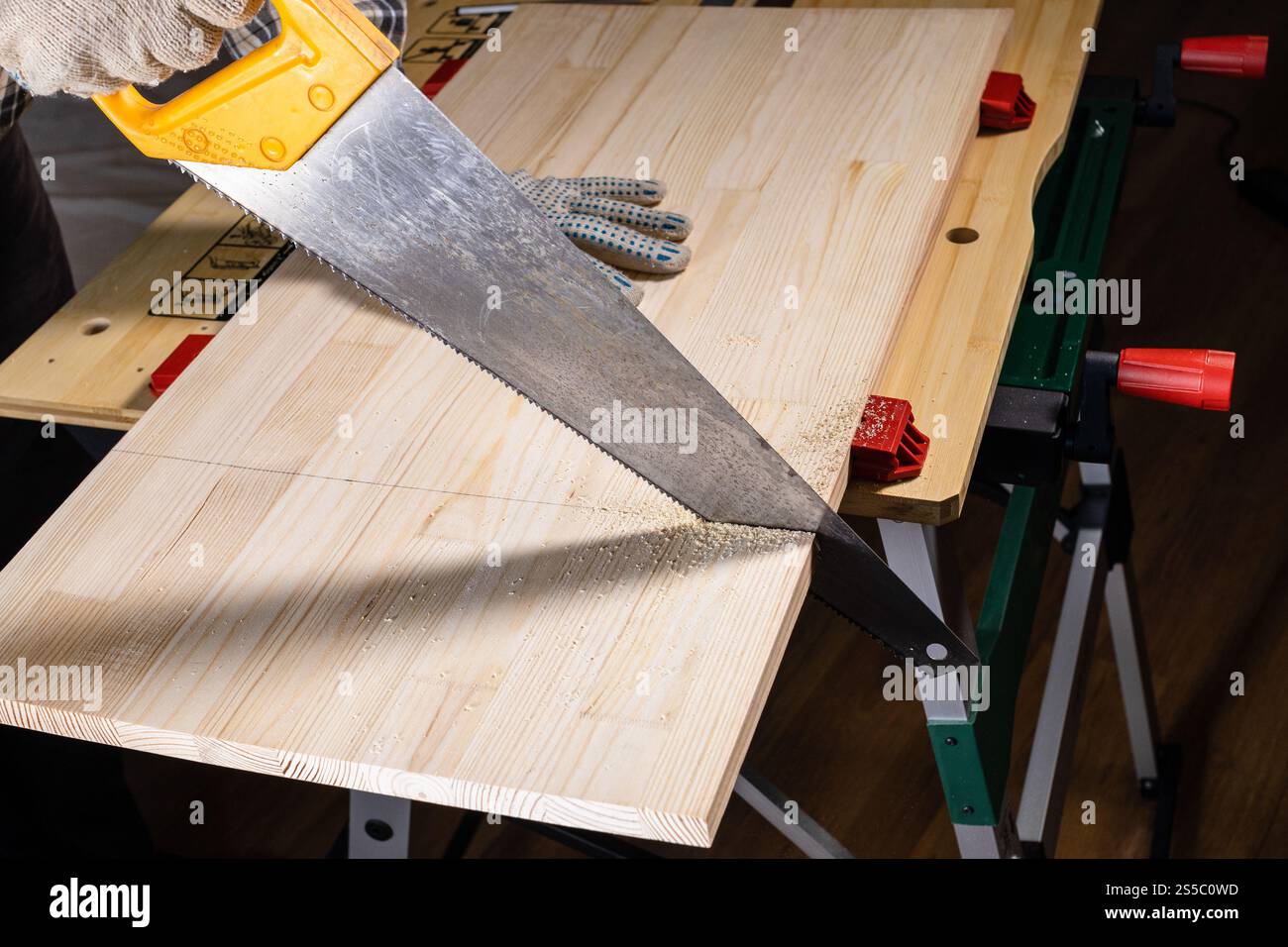side view of sawing wooden board with hand saw on workbench at home ...