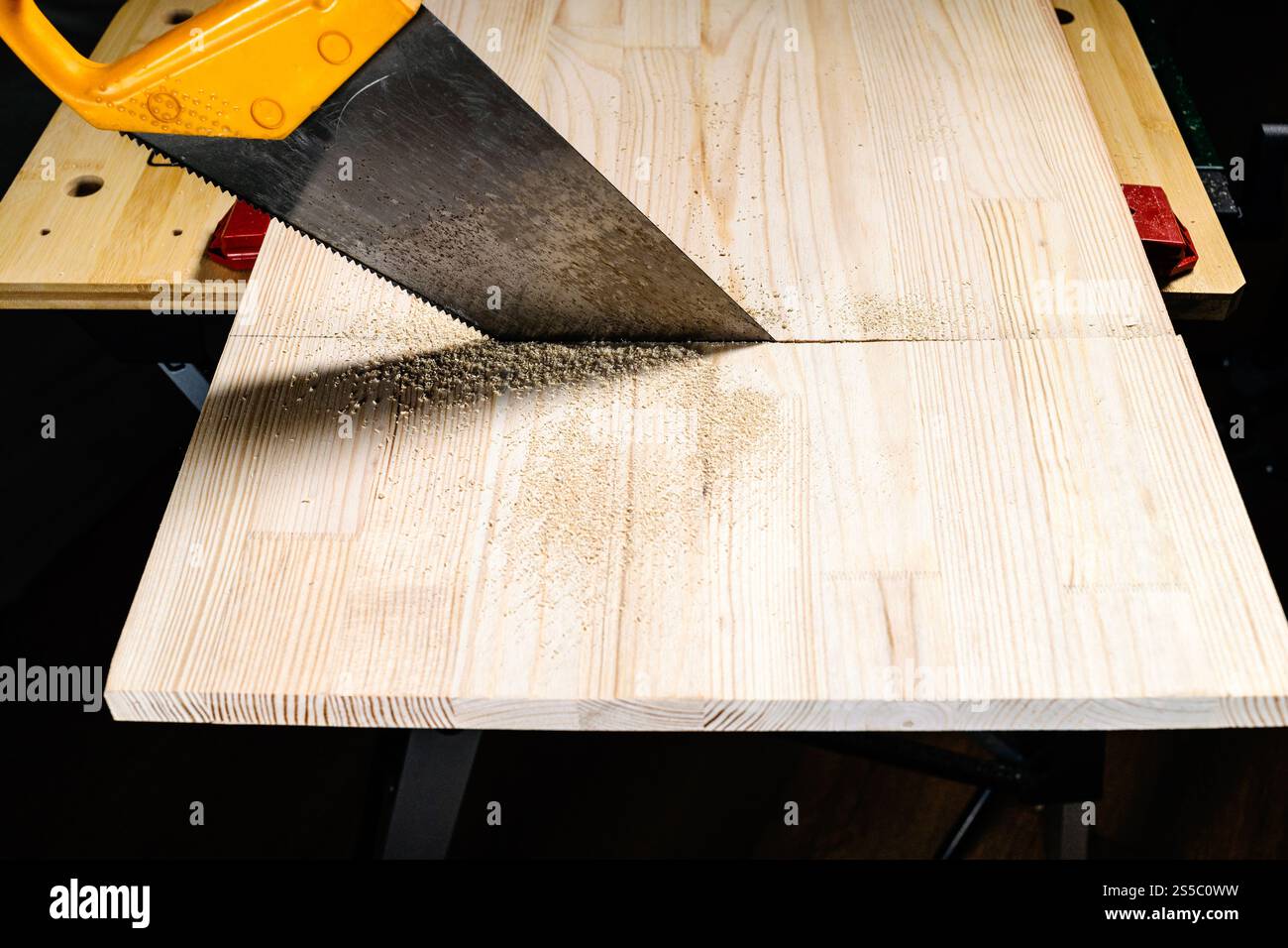 side view of hand saw sawing solid wooden board on workbench at home ...