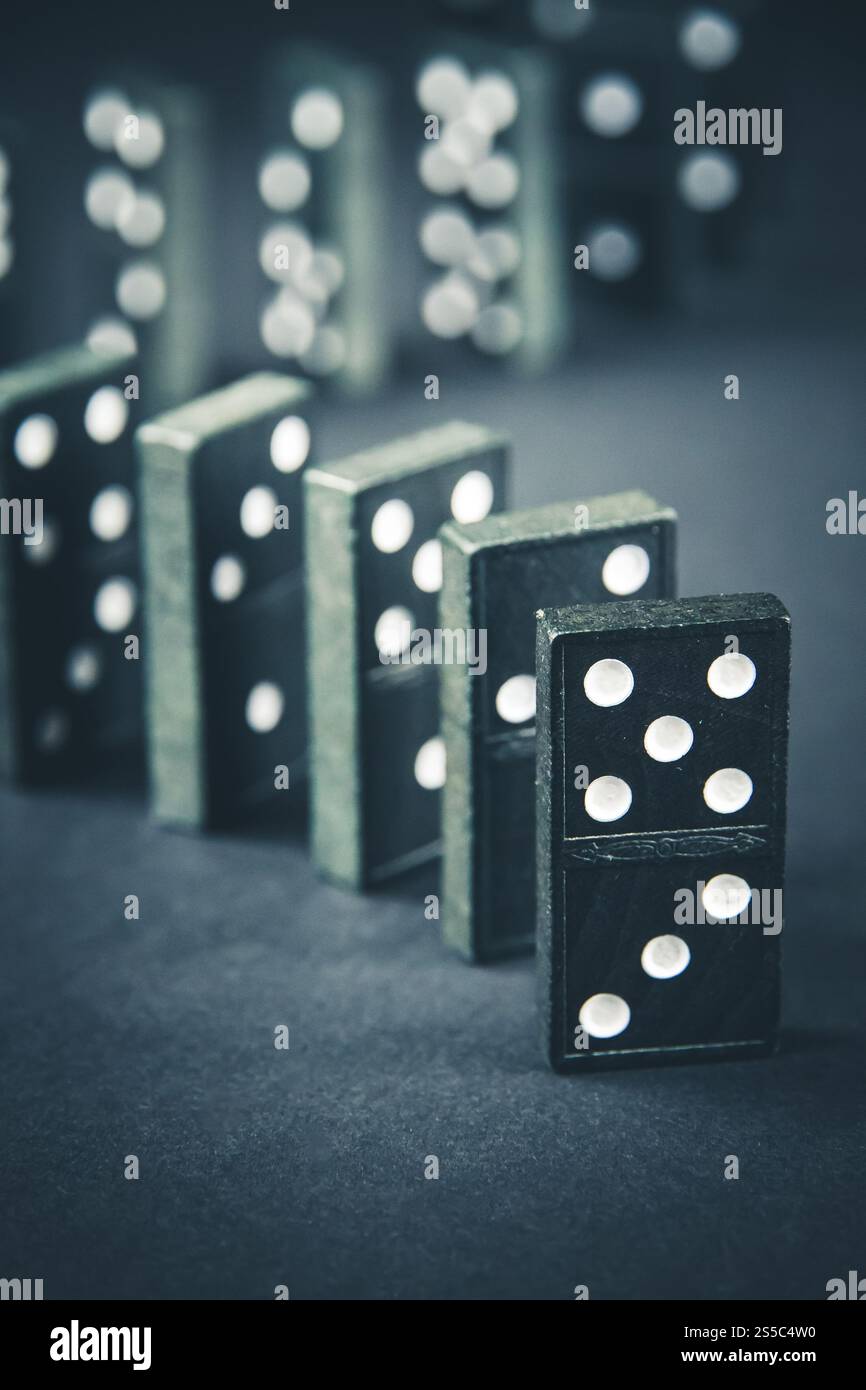 Black dominoes chain on a dark table background. Domino effect concept ...