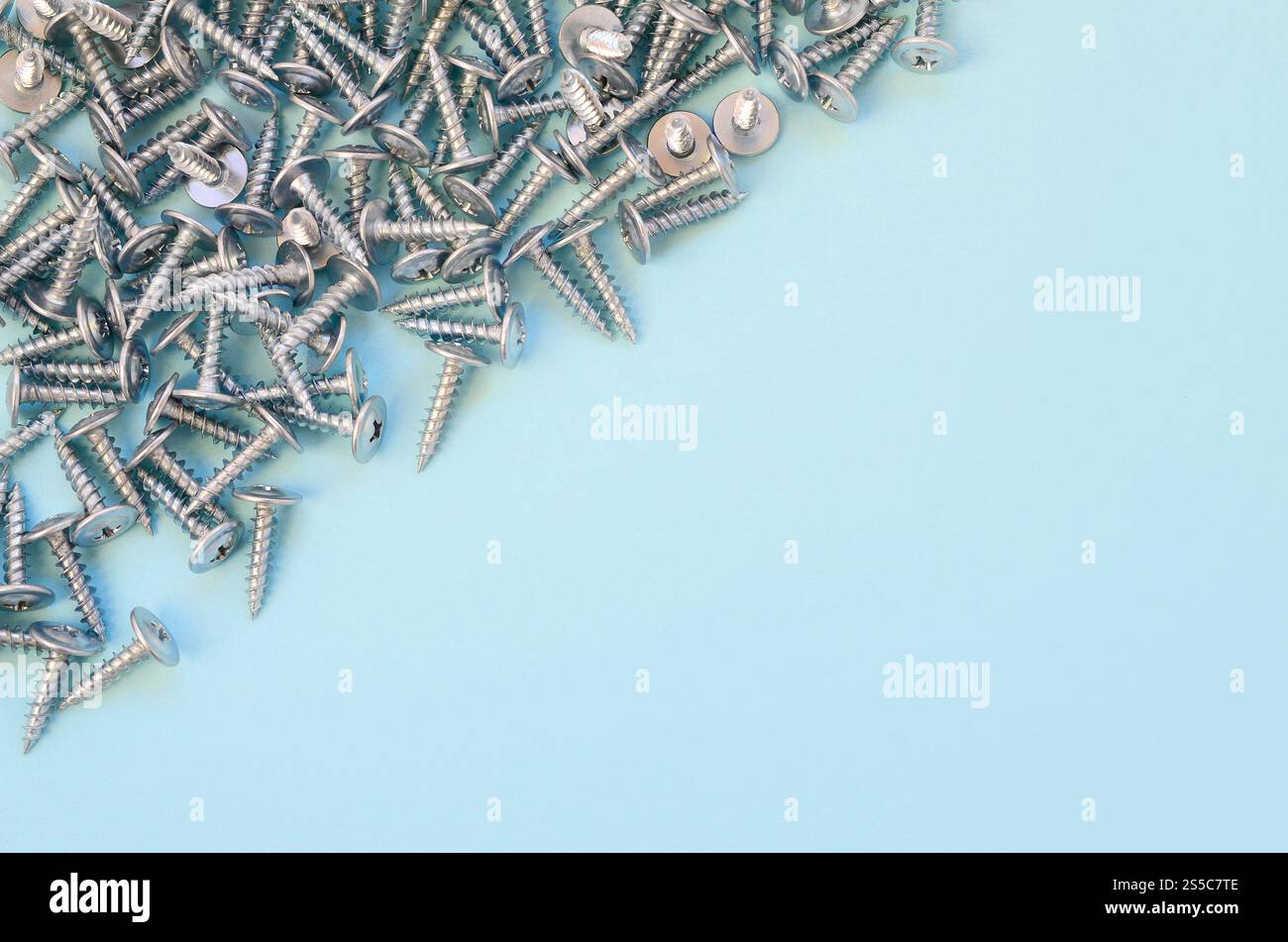 A lot of small silver screws lies on a light blue background. Minimal ...