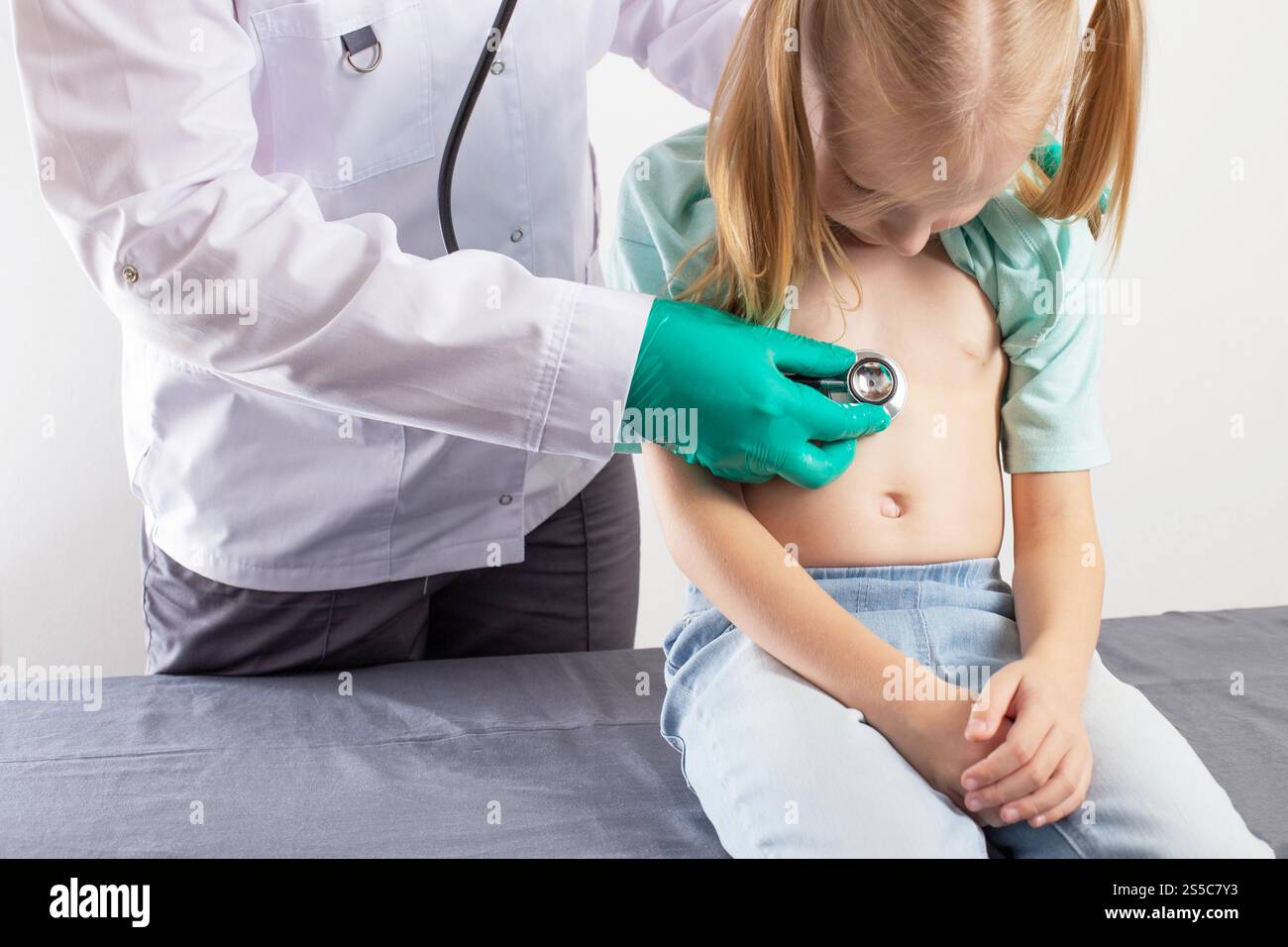 A doctor in green medical gloves listens to the bronchi with a ...