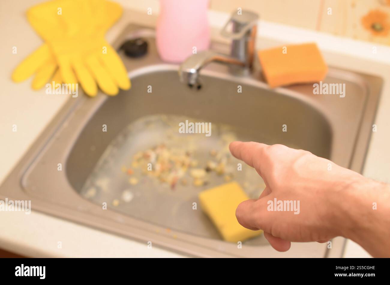 Hand points to dirty kitchen sink with many food particles before the ...