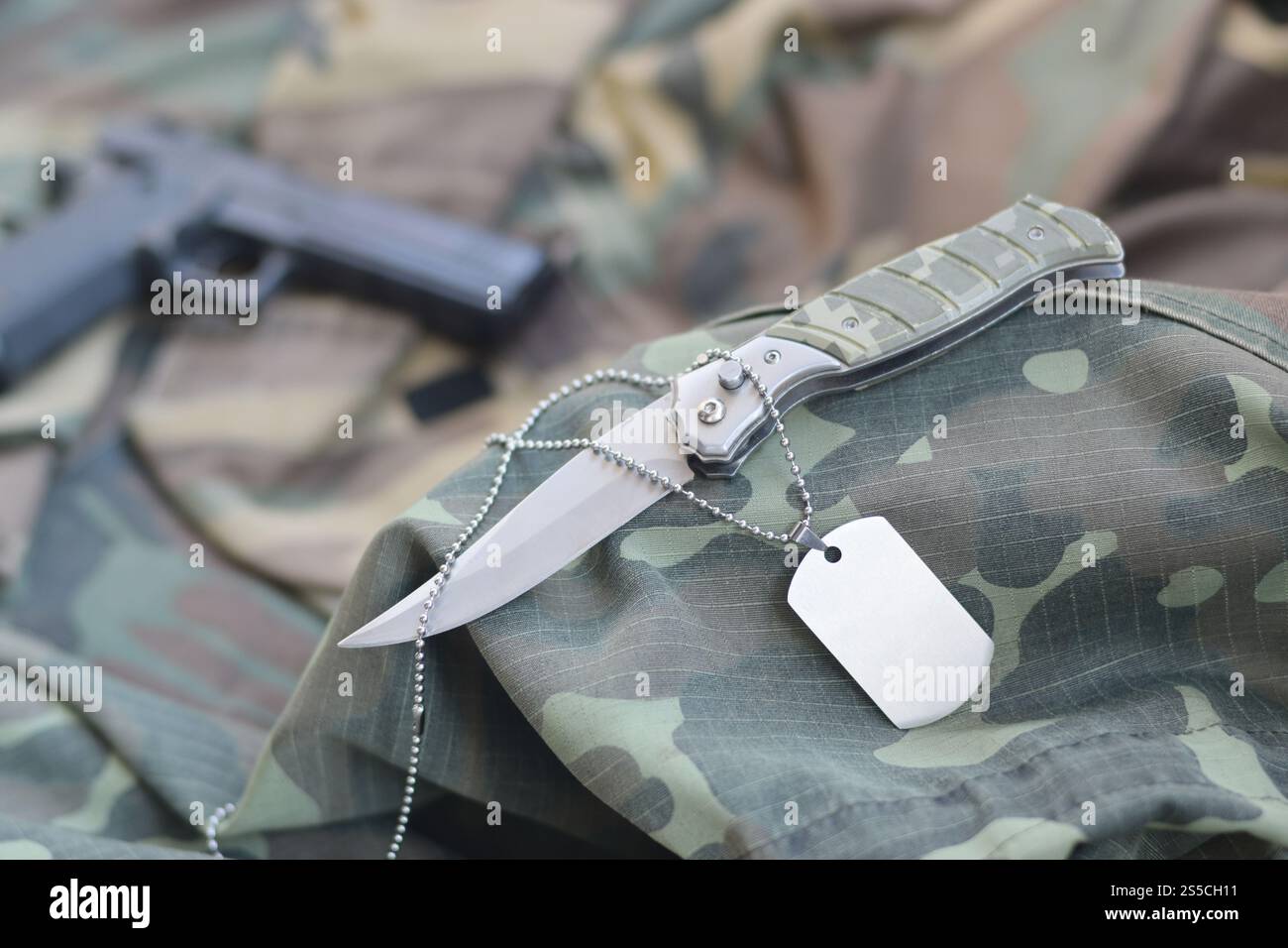 Army Dog tag token with Knife and pistol lie on folded camouflage green ...