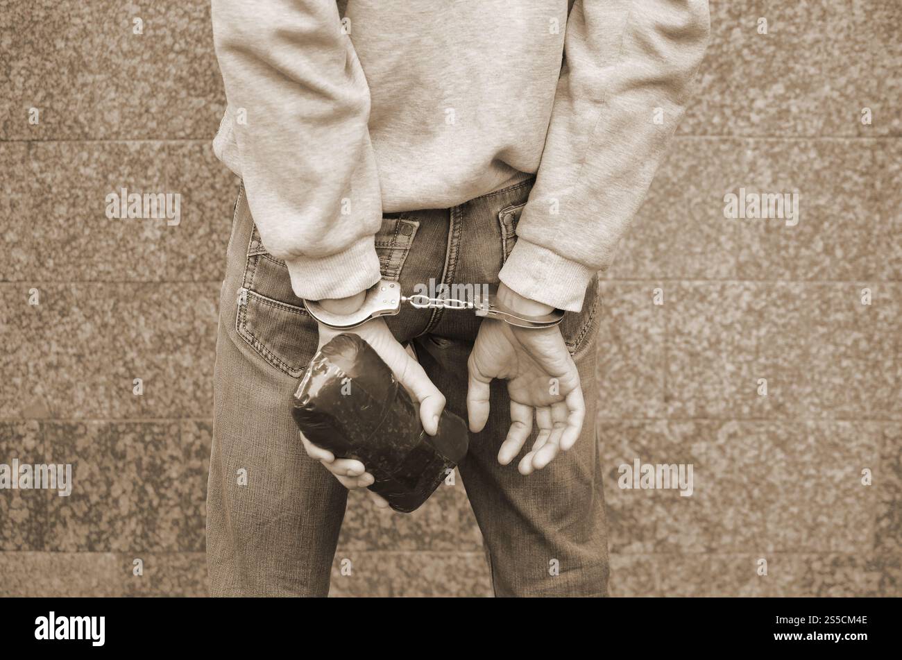 Arrested drug dealer in handcuffs with big heroin drug package on dark ...