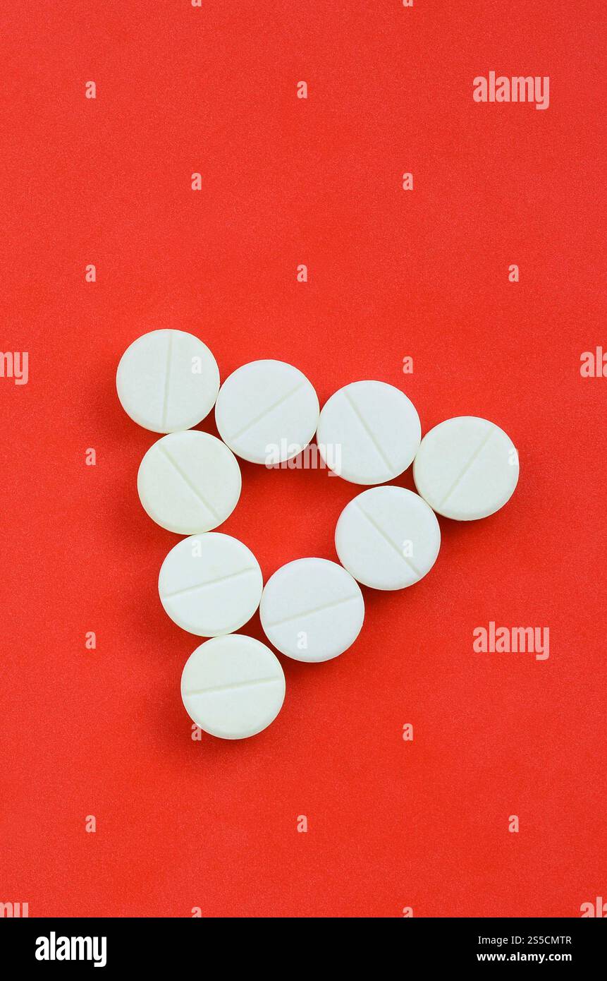 Several white tablets lie on a bright red background in the form of an ...