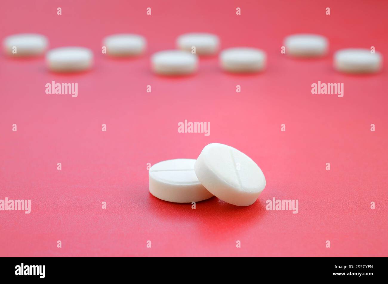 A few white tablets lie on a bright red background surface. Background ...